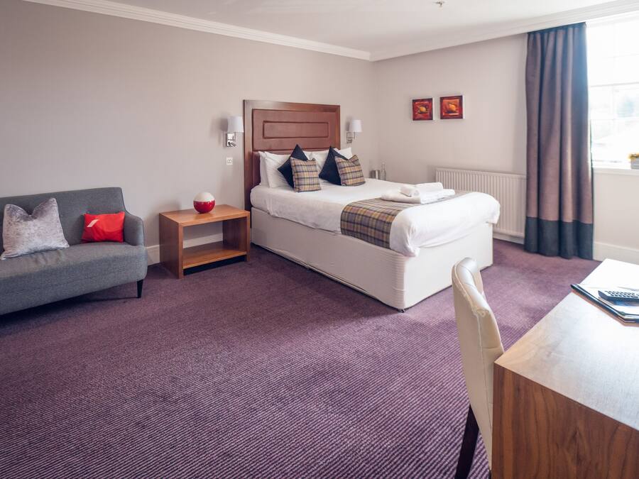 Quarto de hotel com cama, sofá, mesa pequena e cadeira.