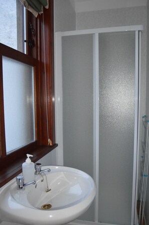 Casa de banho com uma pia branca, um espelho e uma porta de chuveiro em vidro jateado.