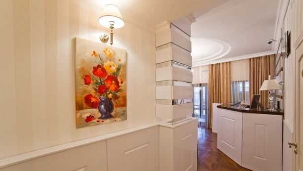 Um corredor com armários brancos, um quadro de flores e uma área de cozinha com bancada e armários.