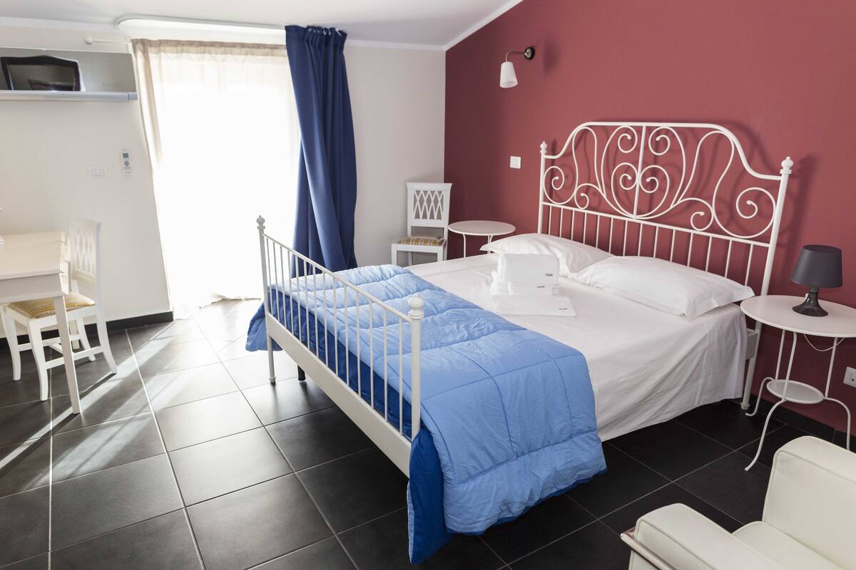 Quarto de hotel com cama, escrivaninha, cadeira, mesinha e abajur.