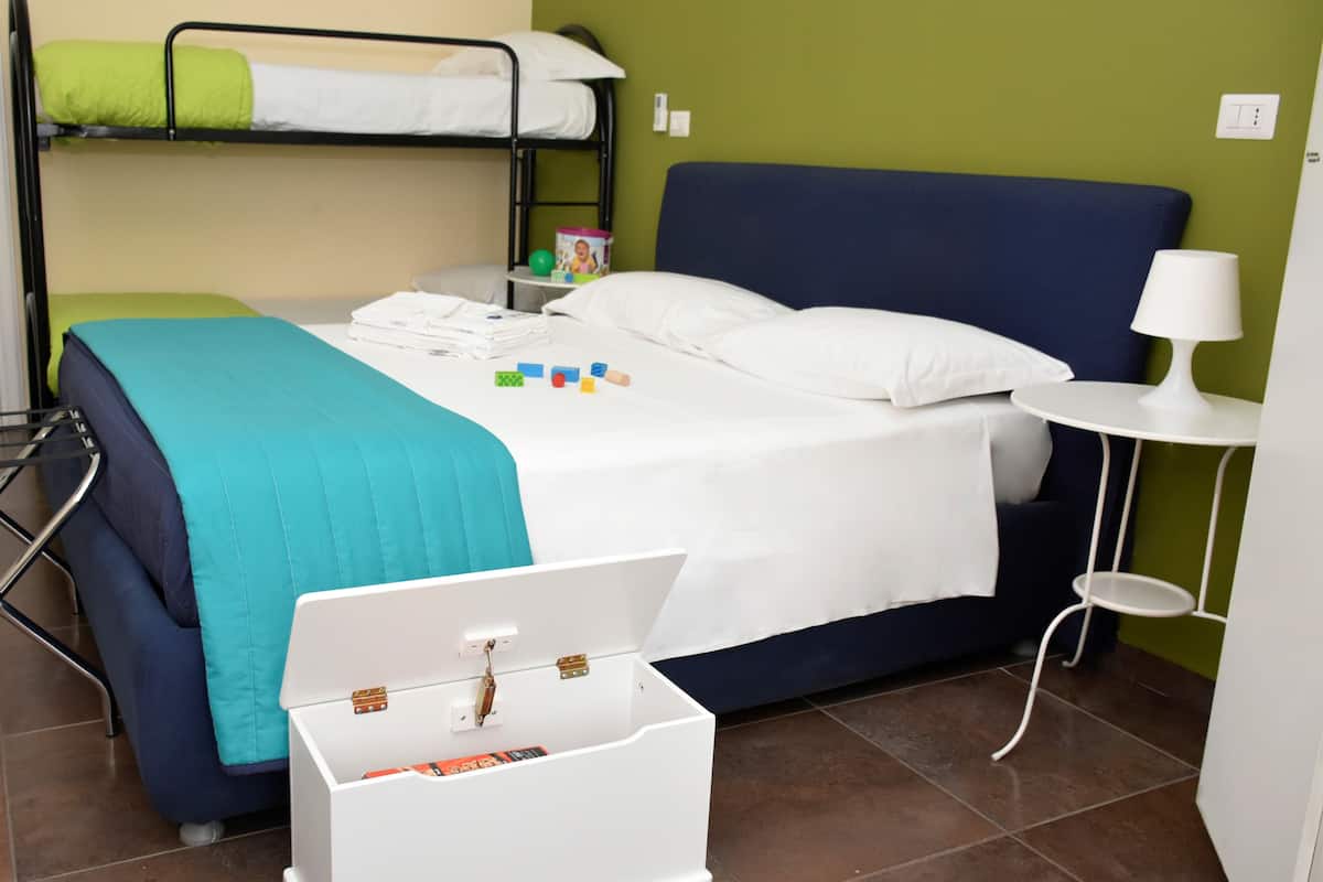 Quarto com beliche, escrivaninha com laptop, pequena mesa com luminária e caixa organizadora.