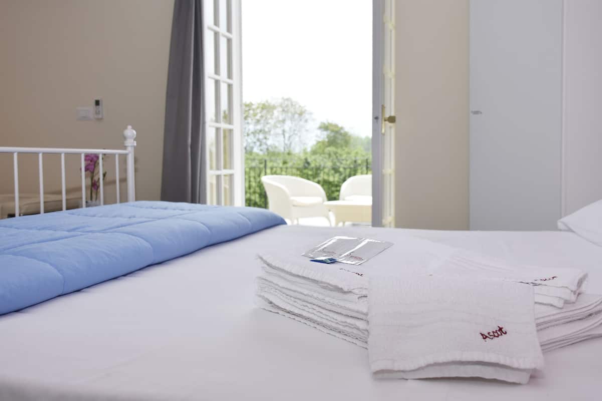 Quarto de hotel com cama, colchão azul, roupa de cama branca e vista para o verde lá fora.