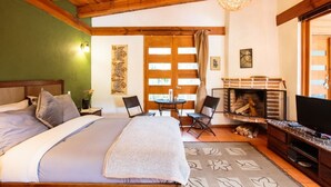 Quarto com cama grande, lareira, televisão e área de jantar com cadeiras.