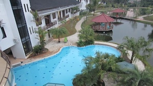 Uma piscina de borda curva, rodeada por palmeiras e um gazebo.