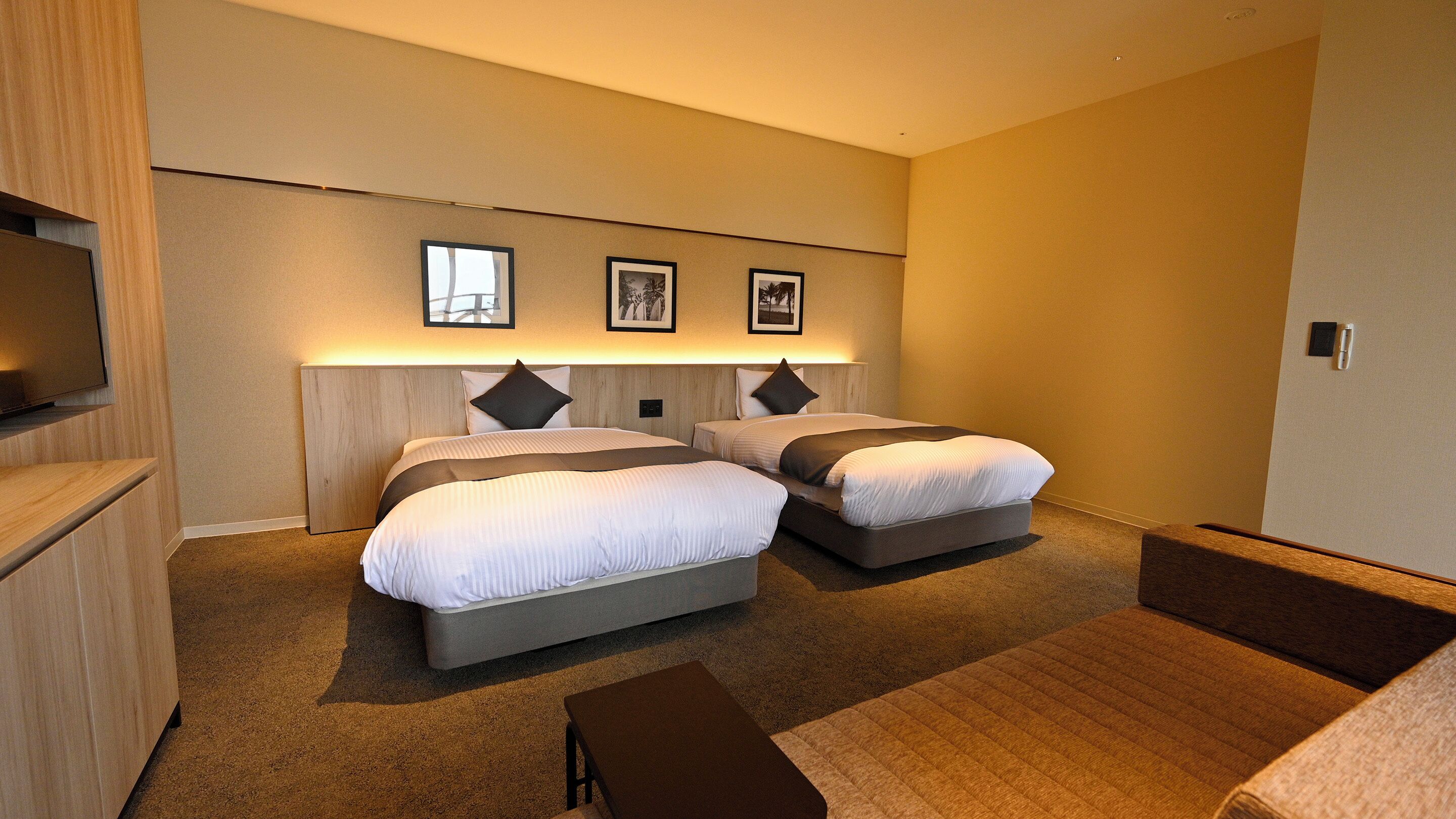 Quarto de hotel com duas camas, uma televisão de tela plana, uma escrivaninha e um pequeno espaço de estar.