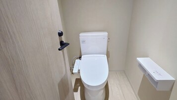 Uma casa de banho pequena e limpa, com sanita branca, lavatório fixado na parede e porta com puxador.