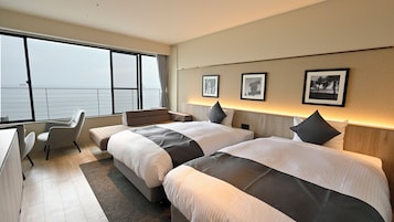 Quarto de hotel com duas camas, uma escrivaninha e vista para o mar.