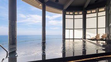 Uma piscina infinita com vista para o oceano, uma área de estar com cadeiras e um design arquitetônico moderno com grandes janelas.
