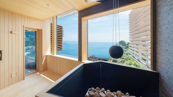 Interior moderno com painéis de madeira, piso aquecido preto e grandes janelas com vista para o mar.