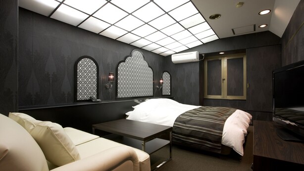 Quarto de hotel moderno com cama, sofá, mesinha e televisão.
