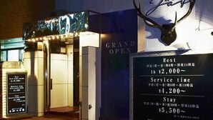 Entrada de um hotel com uma placa indicando 'Grand Open' e um letreiro de neon acima da porta.