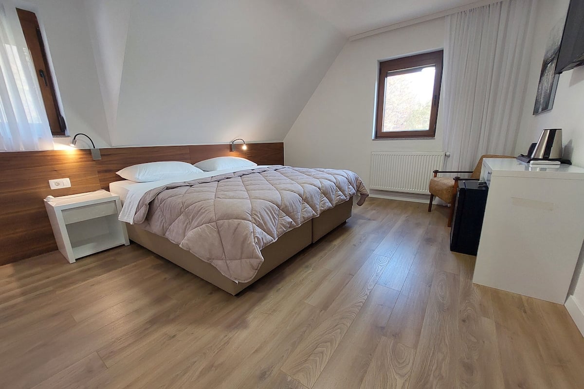 Quarto com cama, mesas de cabeceira, radiador, janela e escrivaninha.