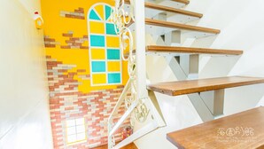 Uma escadaria com degraus de madeira e corrimãos brancos, conduzindo a um patamar com uma parede amarela e uma janela.