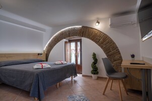 Quarto com cama, escrivaninha, cadeira, planta em vaso e porta em arco.