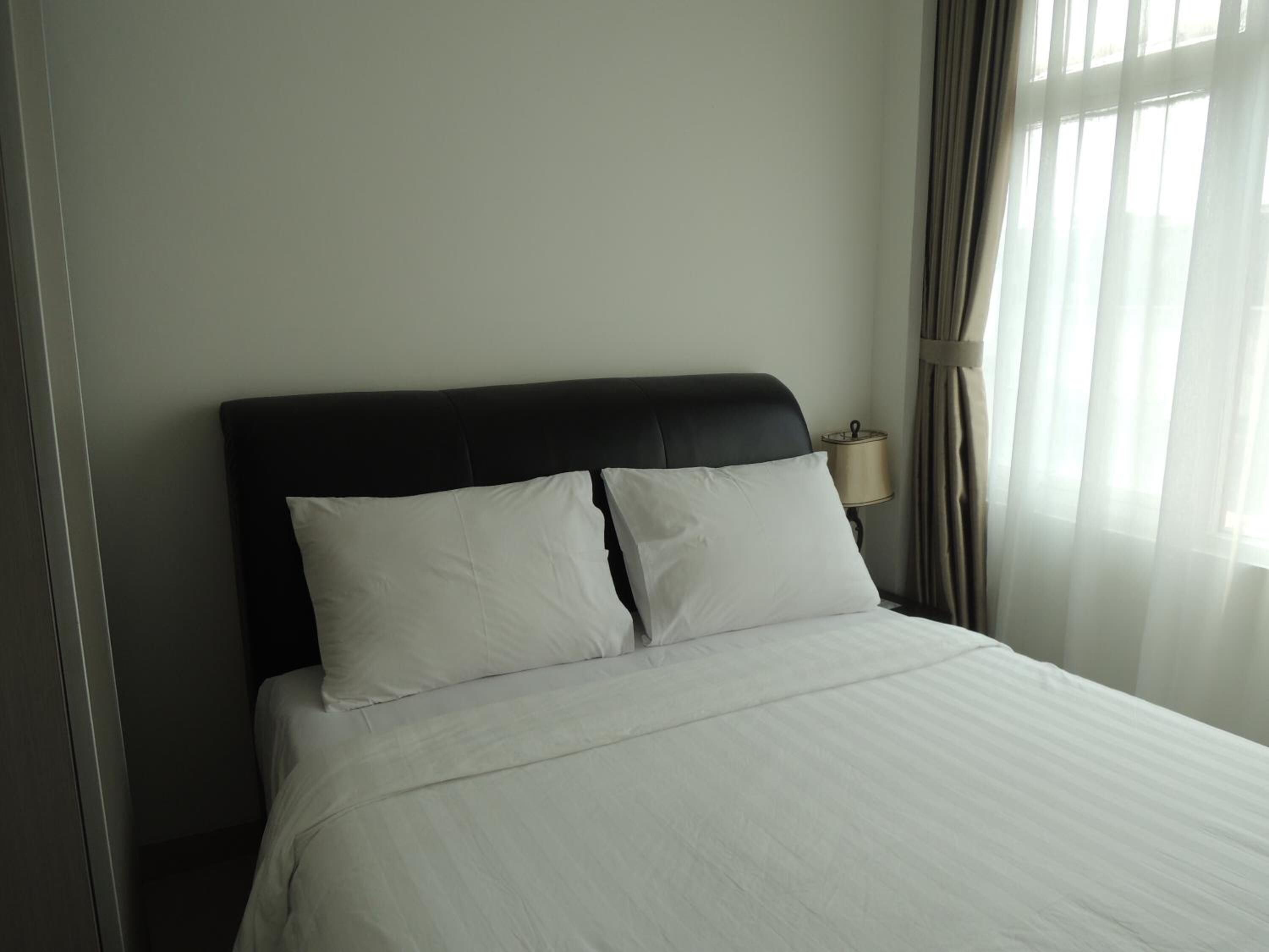Cama bem arrumada com lençóis brancos, cabeceira preta e abajur.
