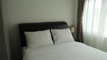 Cama bem arrumada com lençóis brancos, cabeceira preta e abajur.