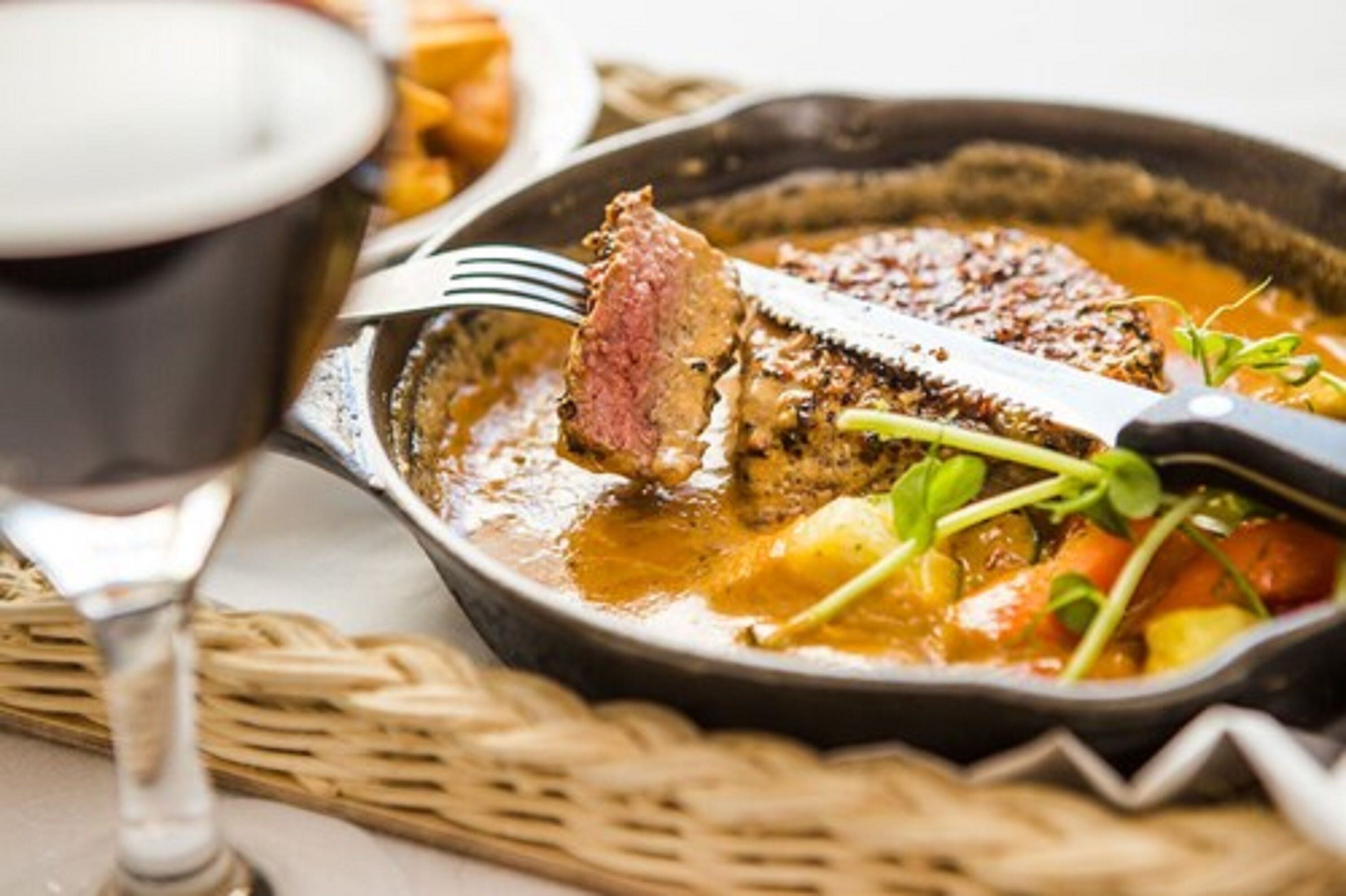 Bife na frigideira com legumes e um copo de vinho.