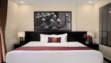 Quarto de hotel com uma cama grande, duas mesas de cabeceira com luminárias, uma obra de arte emoldurada sobre a cama e uma janela com persianas.