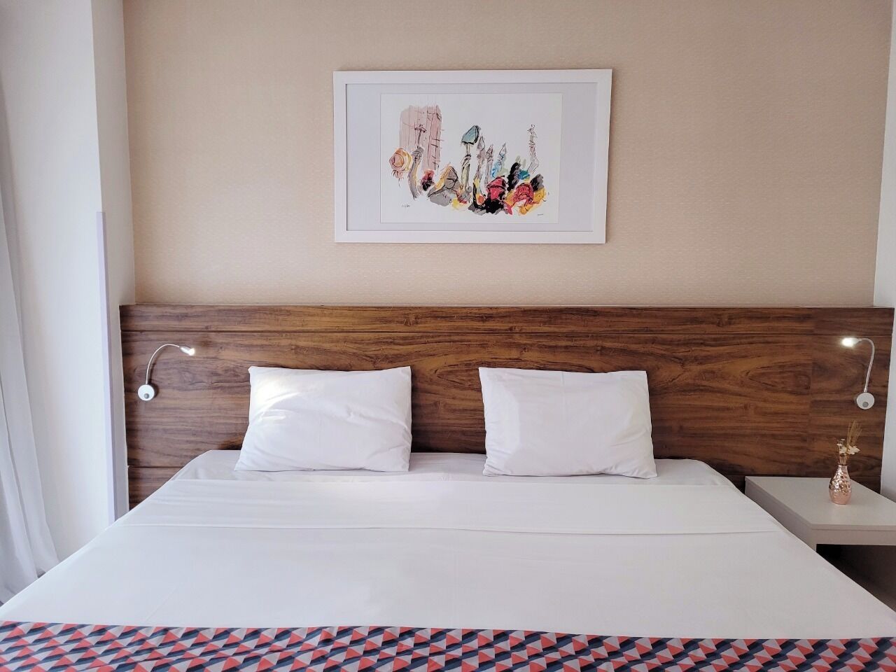 Uma cama bem arrumada com lençóis brancos, cabeceira de madeira e uma obra de arte emoldurada acima.