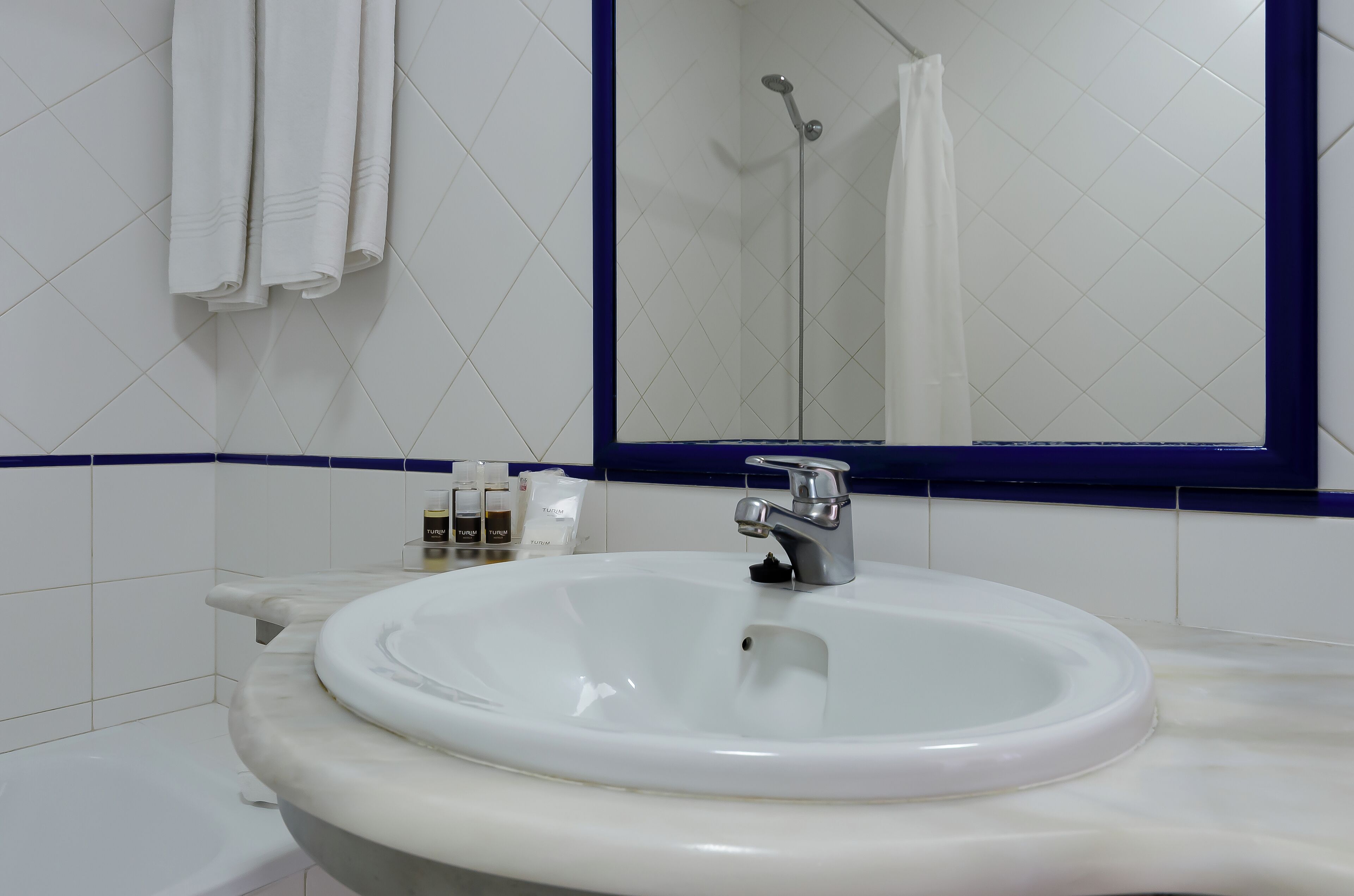 Casa de banho com lavatório branco, espelho e chuveiro.