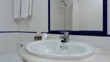Casa de banho com lavatório branco, espelho e chuveiro.