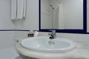 Casa de banho com lavatório branco, espelho e chuveiro.