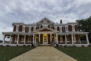 Uma casa grande de dois andares, com entrada central, varanda e fachada simétrica.