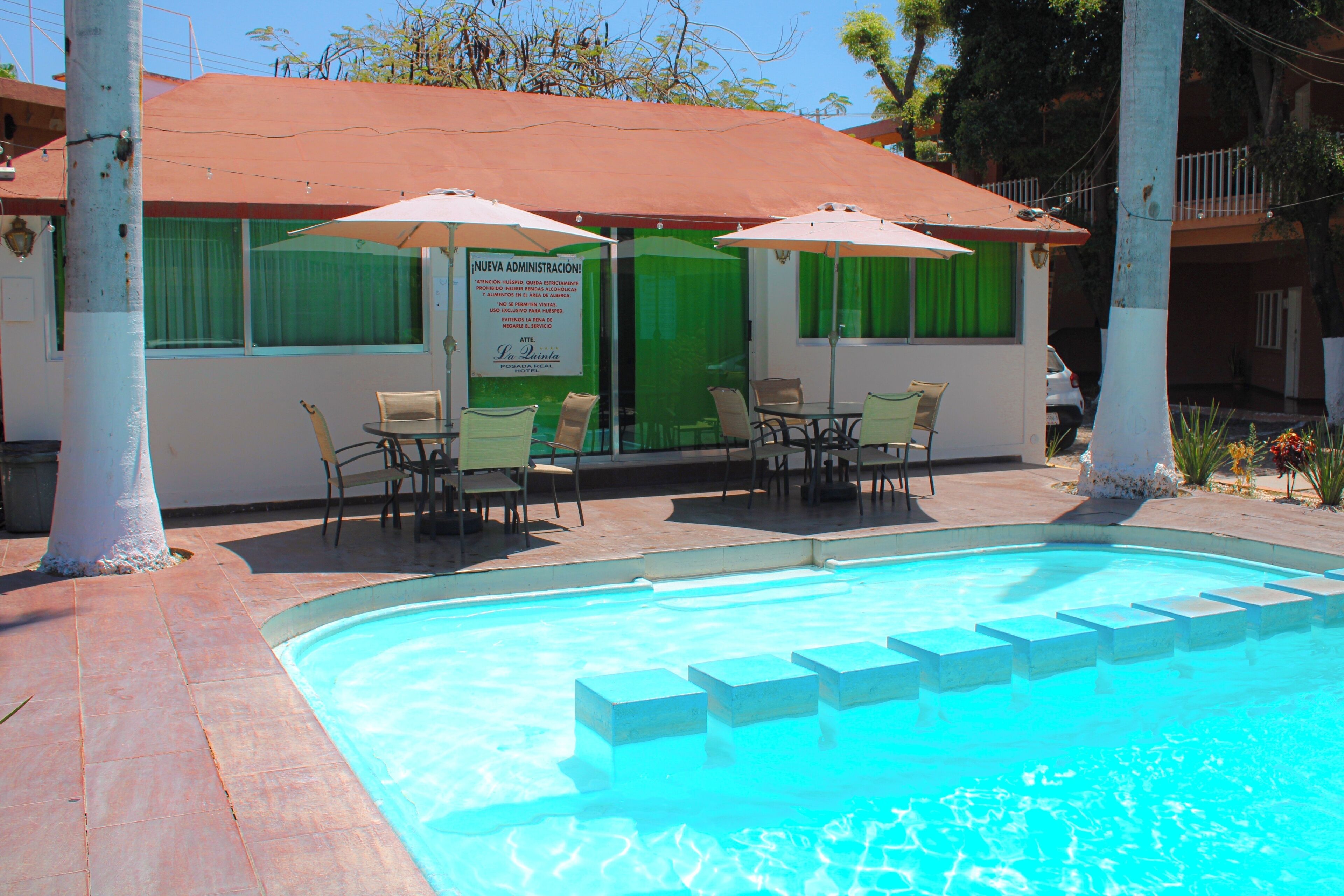 Piscina com degraus de acesso, rodeada por área de estar externa com guarda-sóis.
