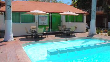 Piscina com degraus de acesso, rodeada por área de estar externa com guarda-sóis.