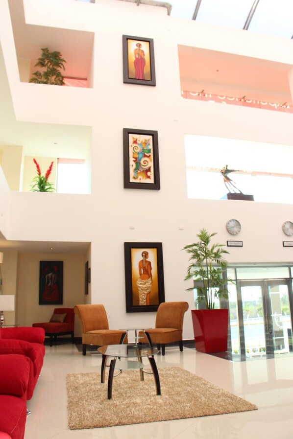Um hall amplo com teto alto, apresentando uma área de estar moderna com sofás e poltronas vermelhas, uma mesa de centro de vidro e um tapete decorativo.