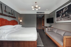Quarto de hotel moderno com uma cama grande, um sofá, uma televisão e um quadro na parede.