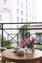 Uma mesa de madeira redonda com uma chávena branca, pires e um vaso de vidro com lírios cor-de-rosa.