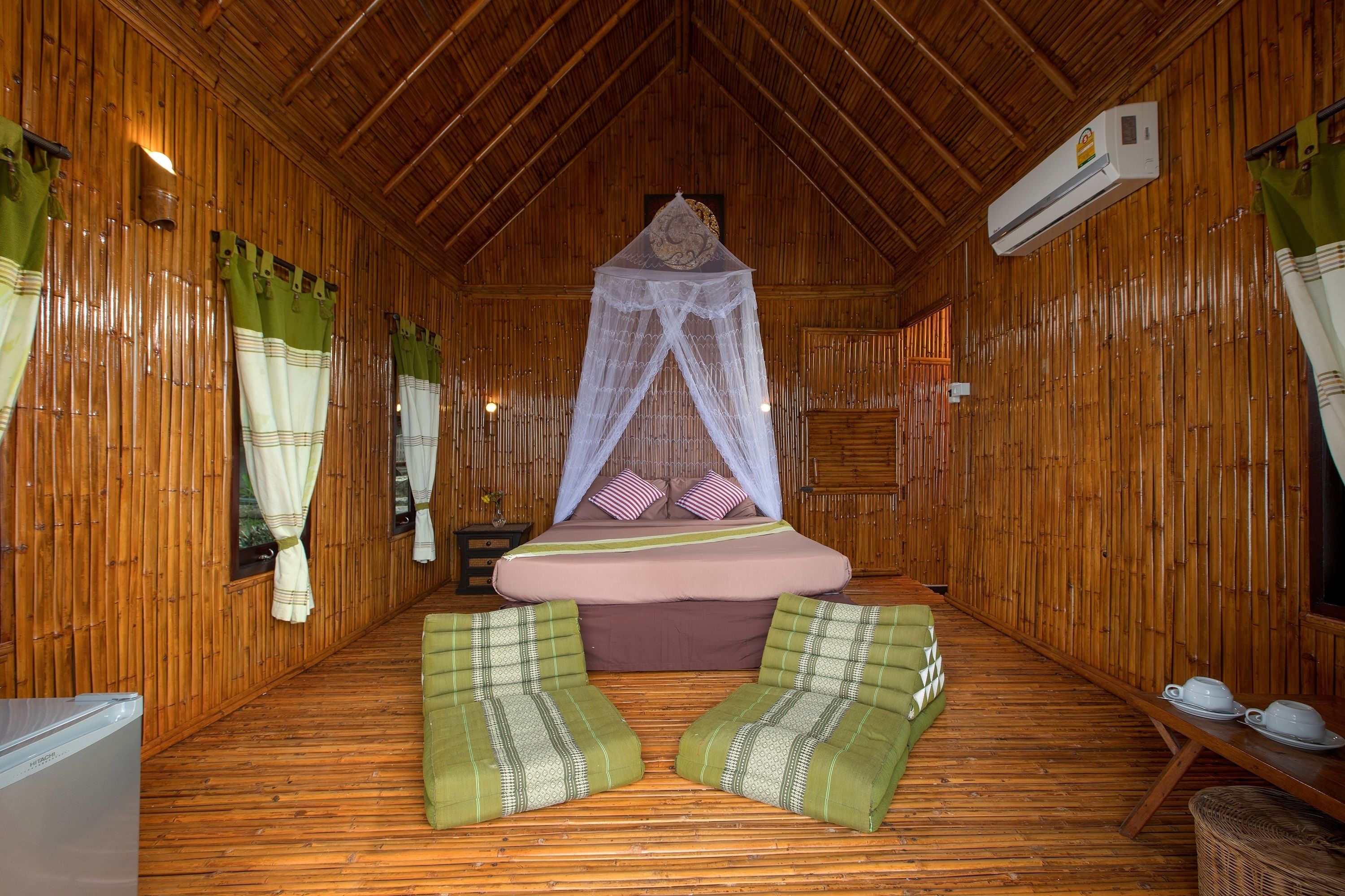 Quarto com uma cama, almofadas verdes, mesa de cabeceira e janela com cortinas.