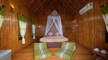 Quarto com uma cama, almofadas verdes, mesa de cabeceira e janela com cortinas.