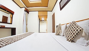 Quarto de hotel com uma cama grande, uma mesa de cabeceira, um espelho e uma porta que dá para outro quarto.