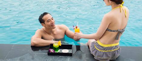 Duas pessoas em uma piscina com bebidas e uma bandeja.