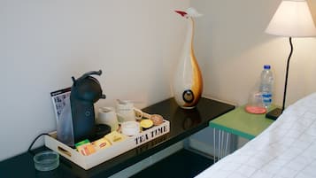 Quarto de hotel com mesa de cabeceira que inclui um tabuleiro para chá, chaleira, luminária e uma garrafa de água.