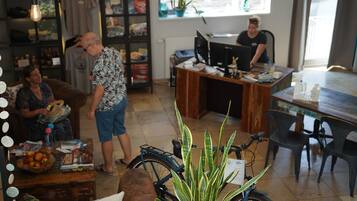 Uma sala de estar com sofá, mesa de centro e uma planta. Há uma bicicleta e uma escrivaninha com um computador.