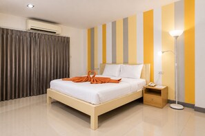Quarto de hotel com cama, mesa de cabeceira com abajur, telefone e parede com listras verticais.