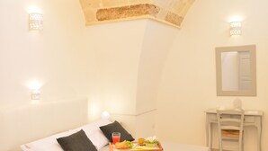 Quarto com cama, mesa de cabeceira e bandeja com frutas e bebida.