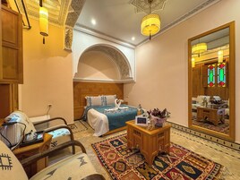 Quarto tradicional marroquino com uma cama, uma mesinha de madeira, um espelho e um tapete estampado.