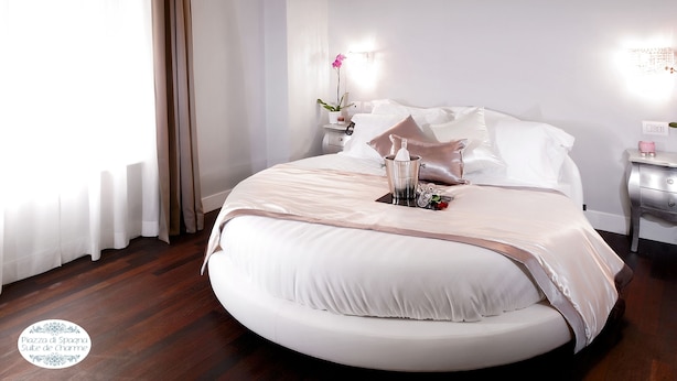 Quarto moderno com cama redonda, mesa de cabeceira, criado-mudo e janela com cortinas.