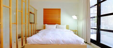 Quarto com estrutura de cama de madeira, uma janela grande com cortinas e um abajur.
