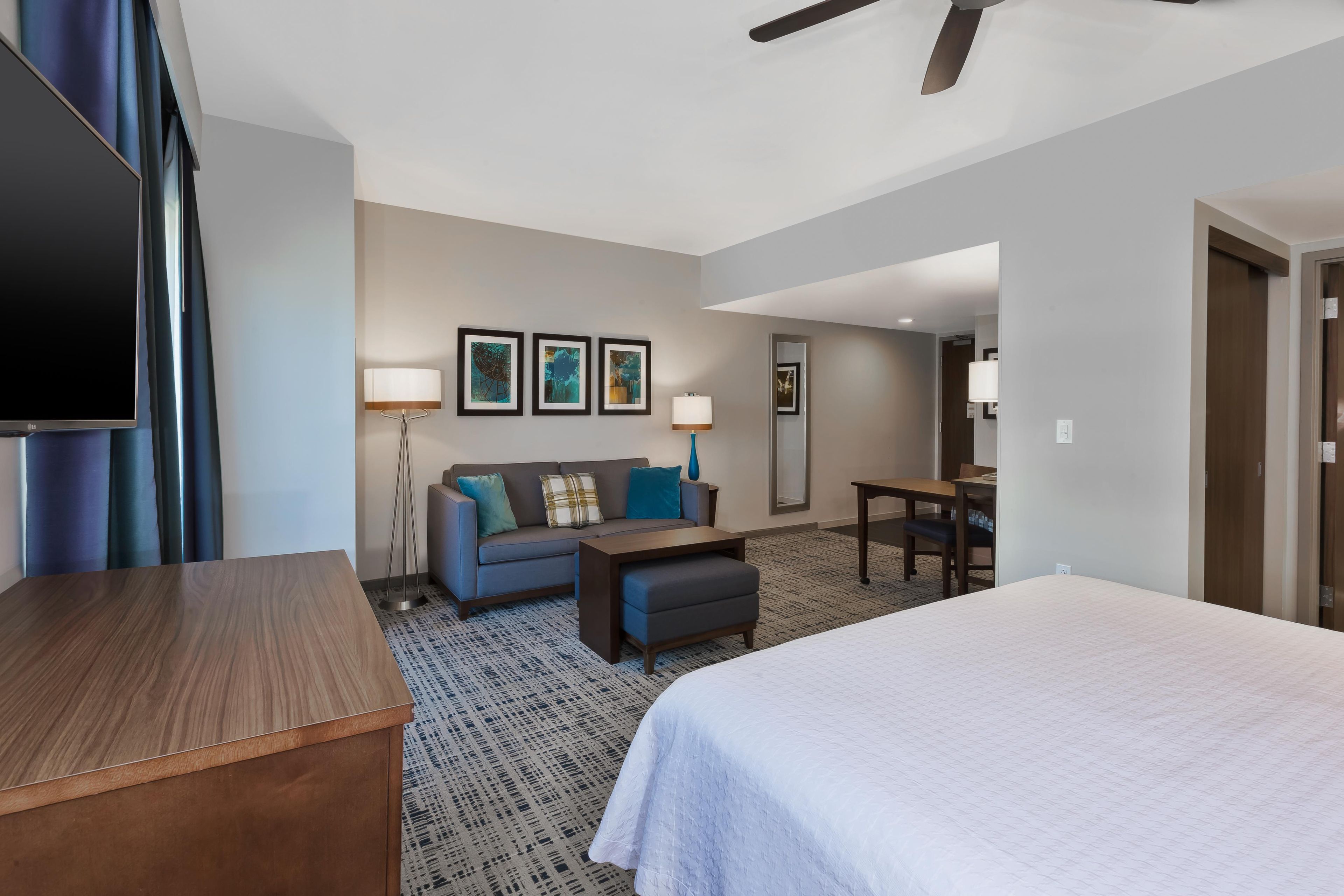 Quarto de hotel com cama, escrivaninha, sofá, televisão e obras de arte na parede.