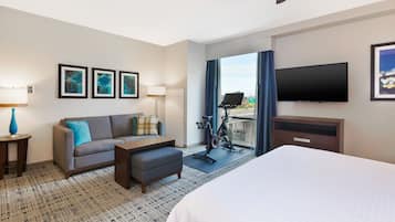 Quarto de hotel com cama, sofá, escrivaninha, televisão e bicicleta ergométrica.