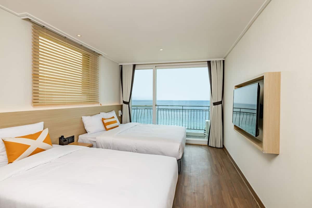 Quarto de hotel com duas camas, televisão e varanda com vista para o mar.