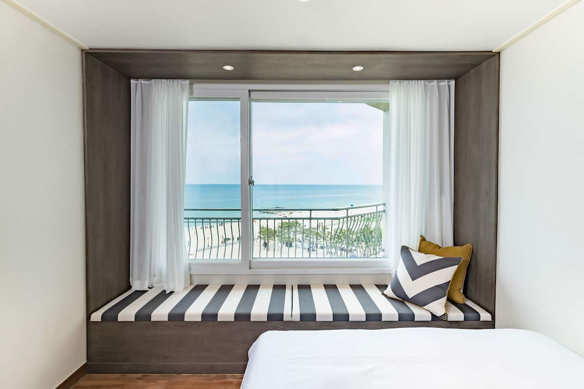 Quarto com uma grande janela, uma cama e vista para a praia.