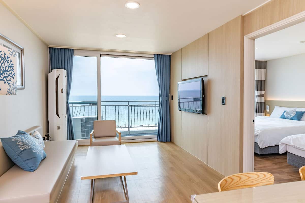 Quarto de hotel com varanda, televisão, sofá, cama e área de refeições.