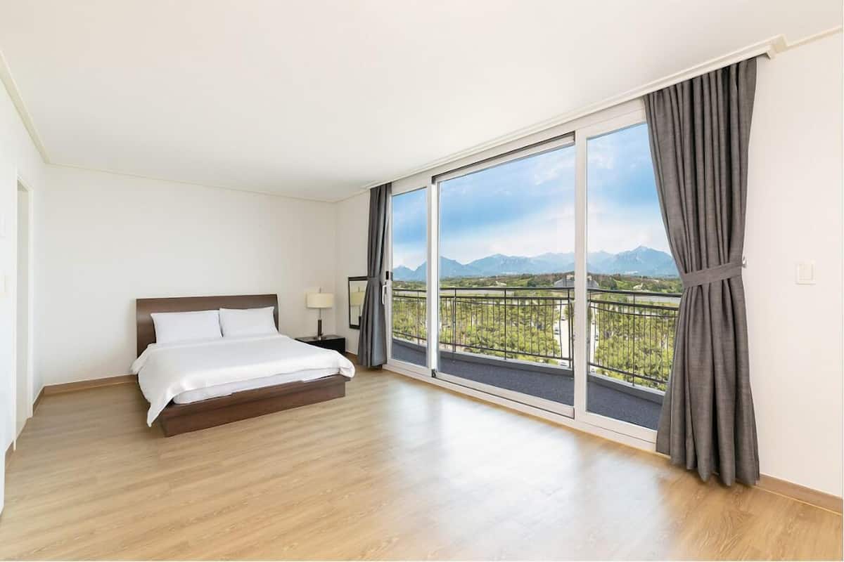 Quarto com uma janela grande, uma cama e uma mesinha de cabeceira.