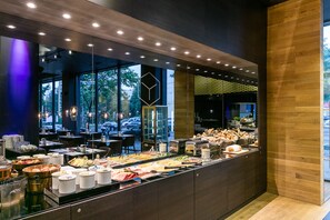 Uma área de buffet com diversas opções de comida, um espaço para sentar e grandes janelas com vista para o exterior.